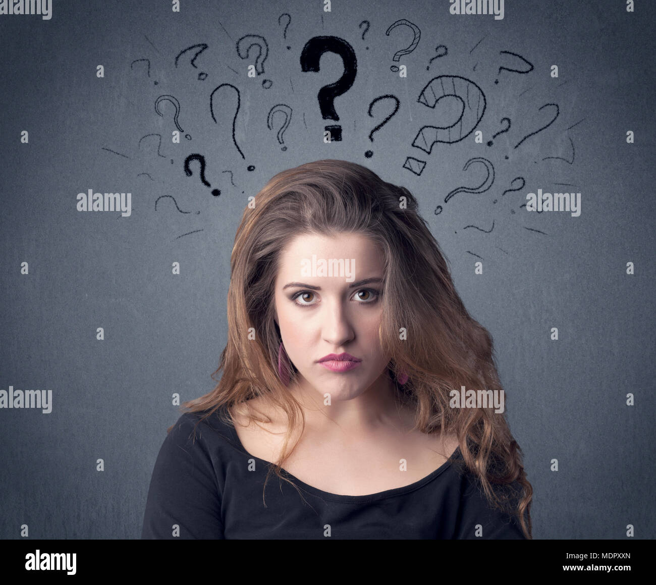 A pretty teenage girl standing confused in front of grey wall ...