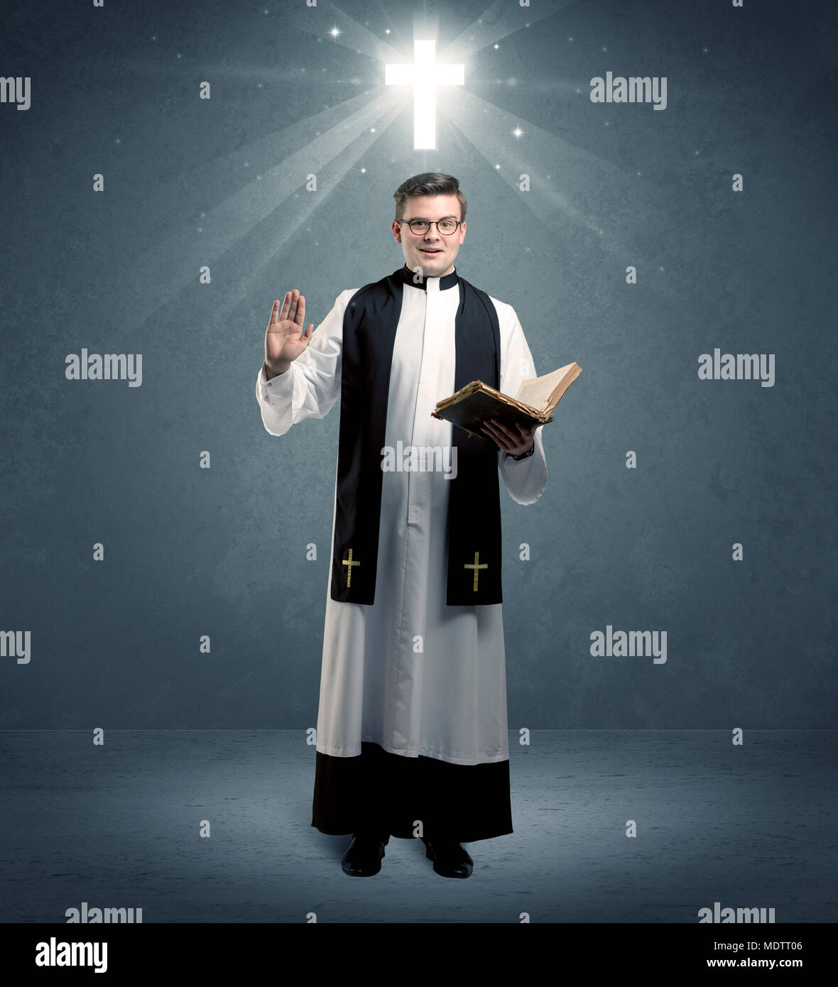 A young caucasian priest with deep faith blessing with the holy bible ...