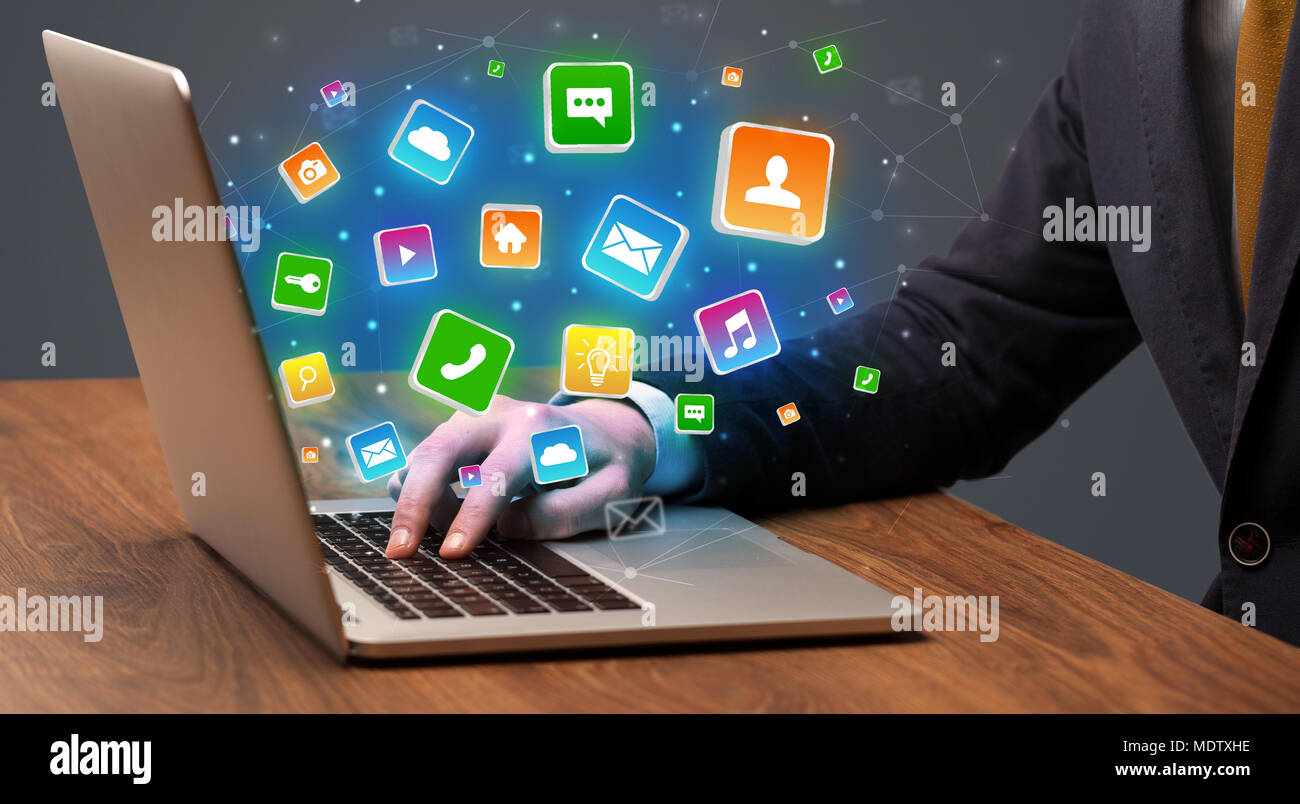 Businessman hand typing on laptop with flying application icons around ...