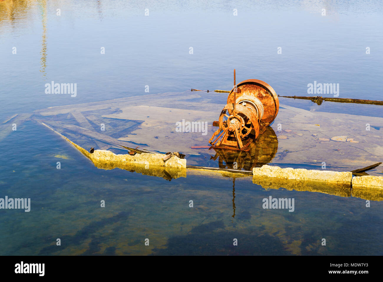 Old wreckage of pram in a small harbor. Parts of rusted winch sticking ...