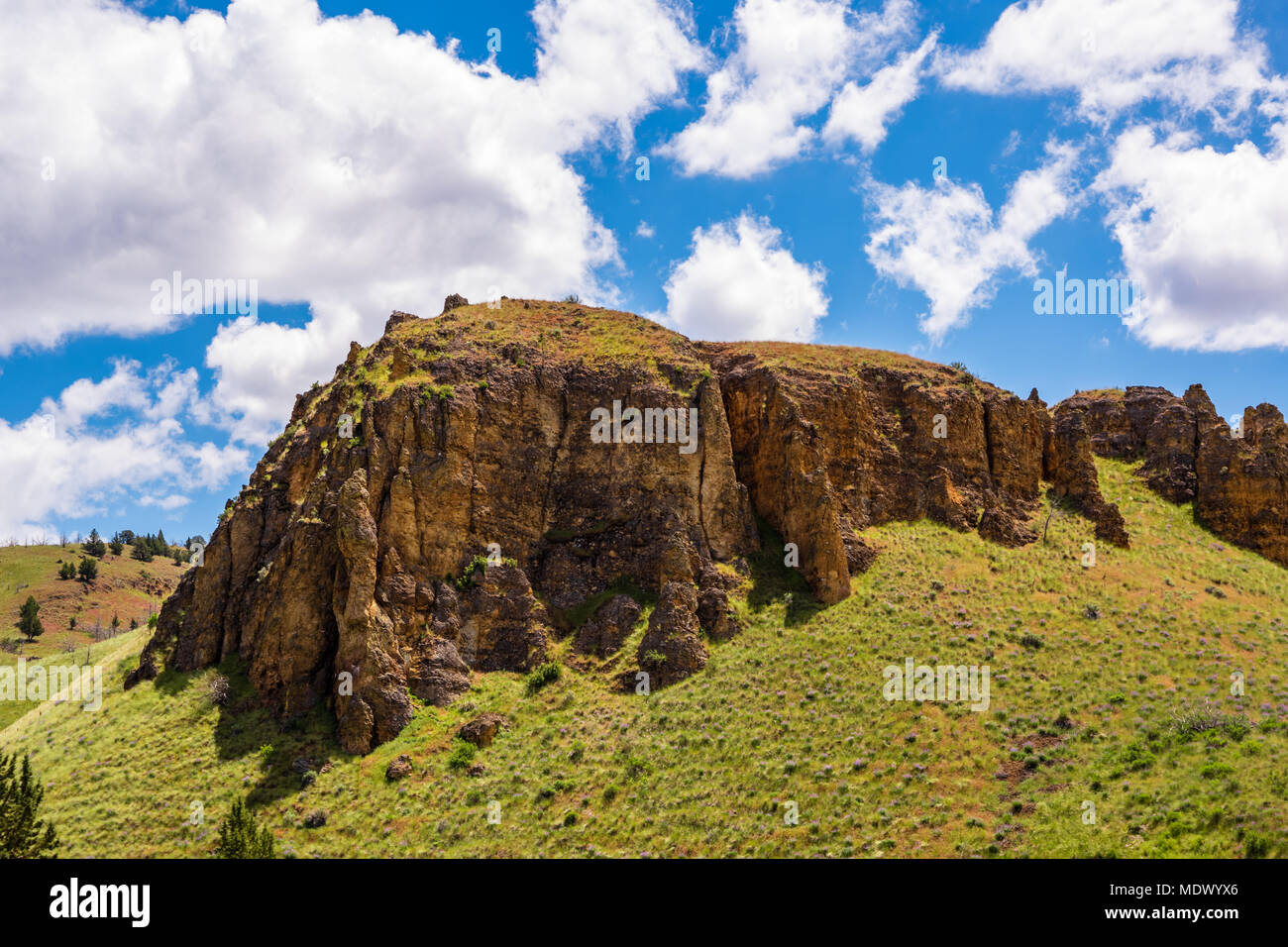 Sharp rock cliffs on a bed of soft grass, blue sky and clouds above ...