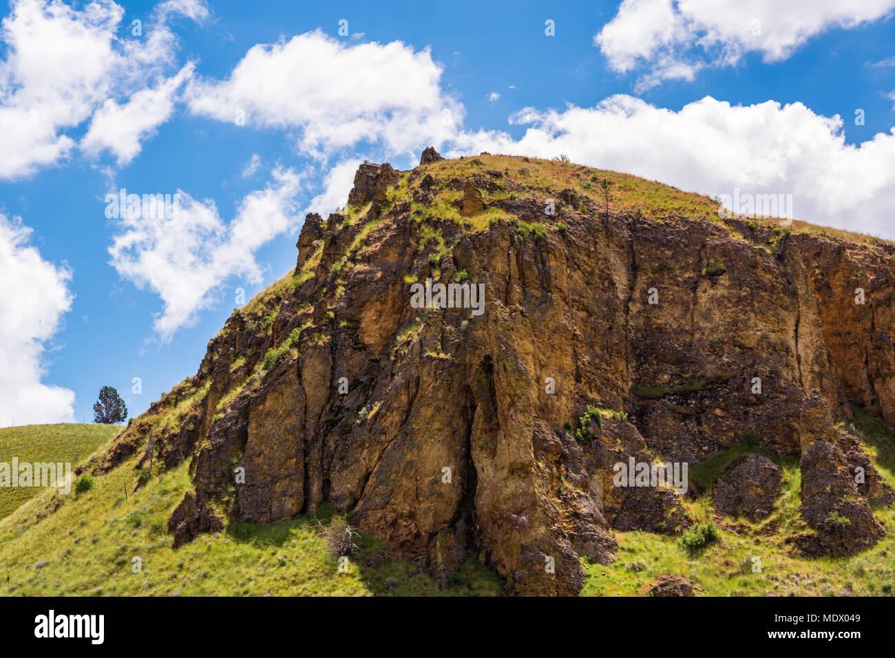 Sharp rock cliffs on a bed of soft grass, blue sky and clouds above ...
