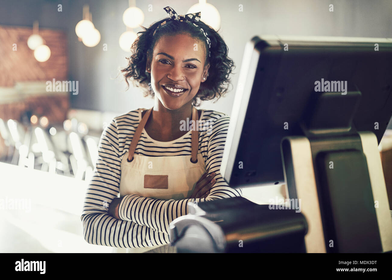 Smiling young African waitress wearing an apron standing by a point of ...