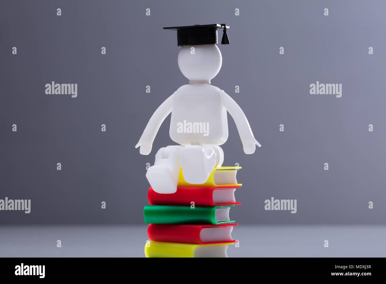 Human Figure With Graduation Hat Sitting On Multi Colored Stacked Books ...