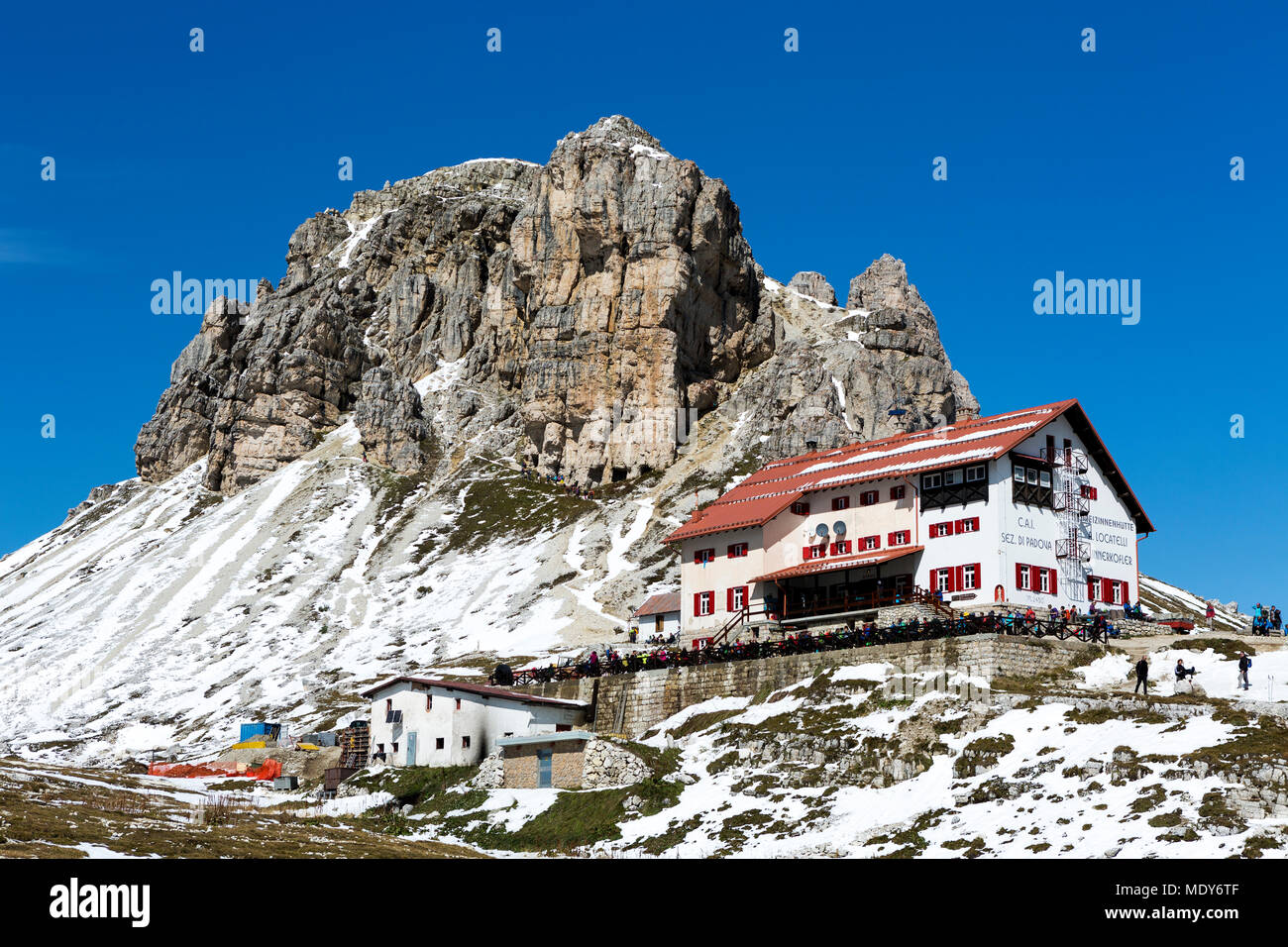 Large mountain hotel on a snow-covered rocky ridge with hikers ...