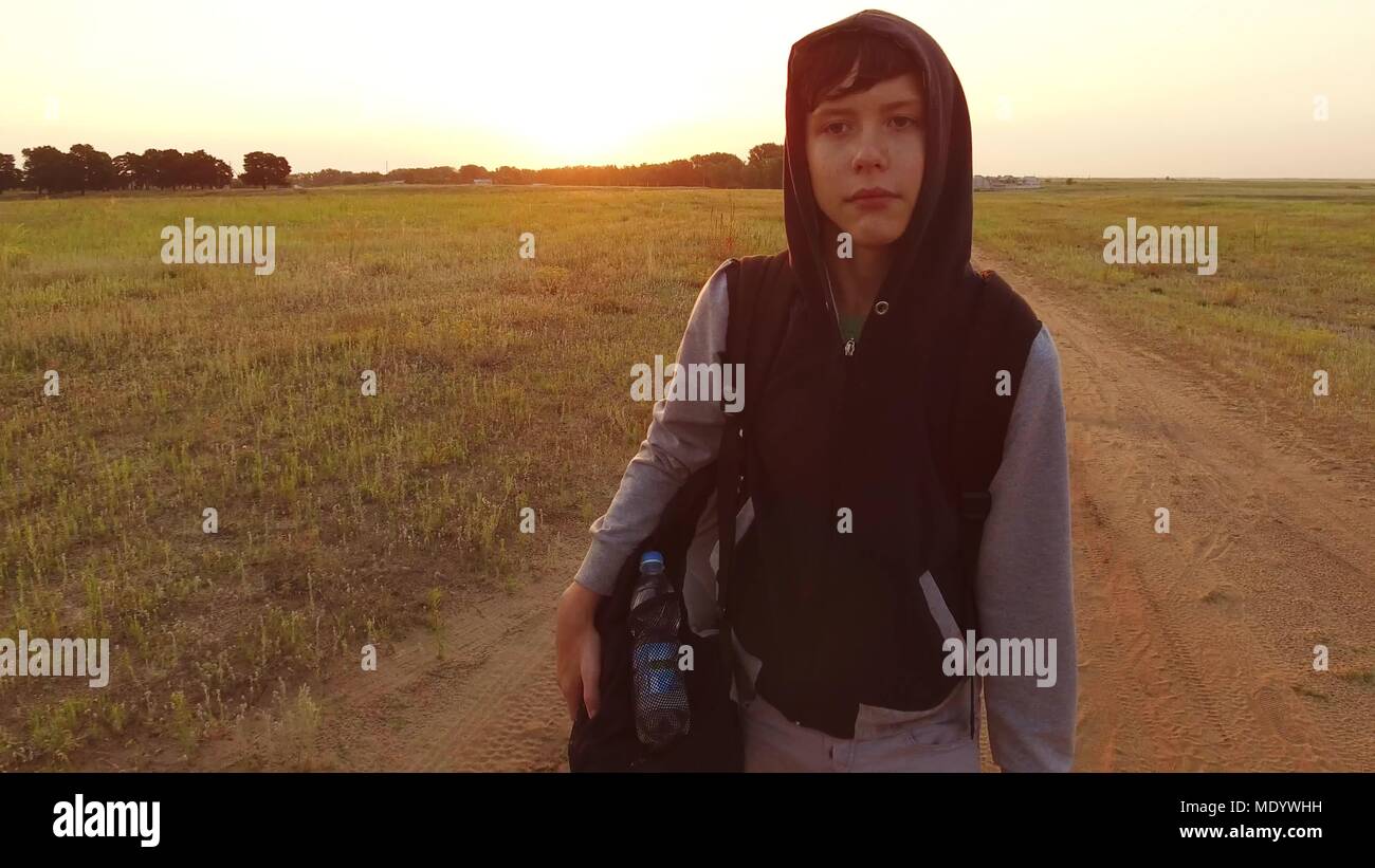 Boy teen traveling. Boy teenage tramp walking along the road in a hood ...