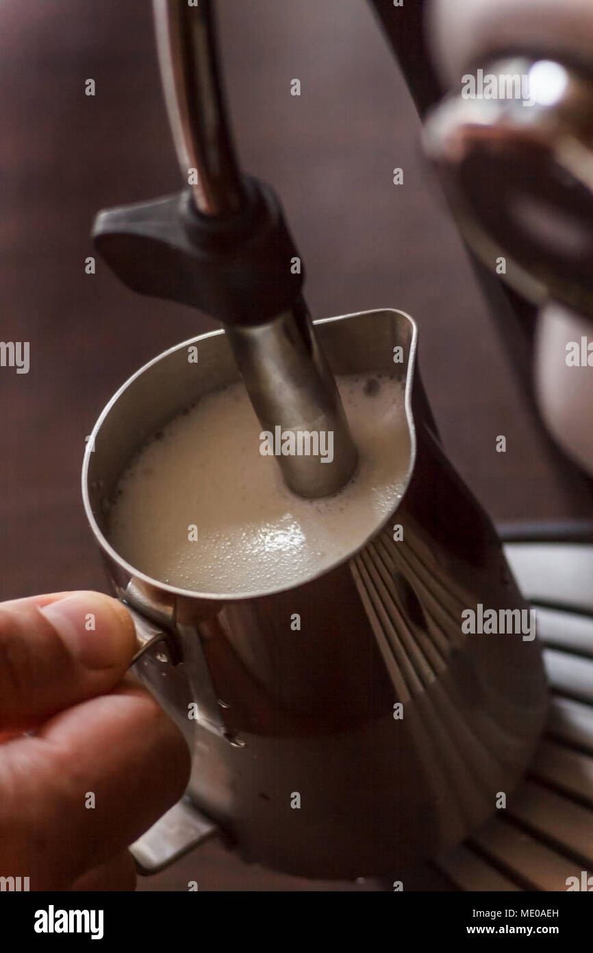 Professional bartender warming milk for cappuccino. Barista using coffee machine for latte art ...