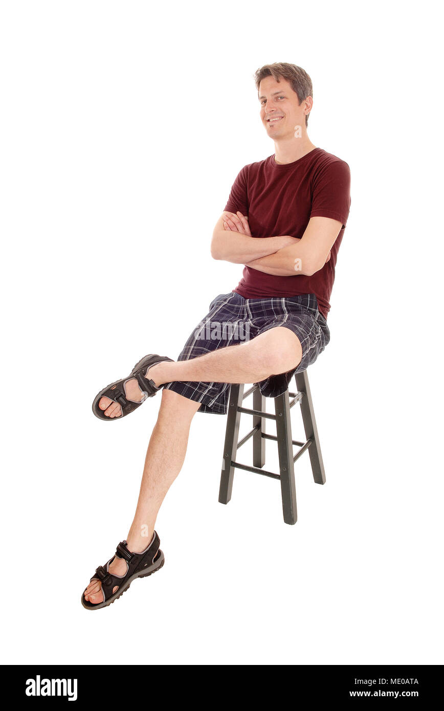 A handsome very happy young man in shorts with his arms crossed sitting ...
