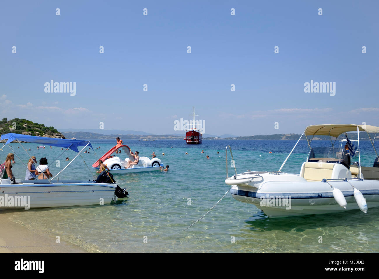 People relaxing in warm shallow water at noon and multiple small boats ...