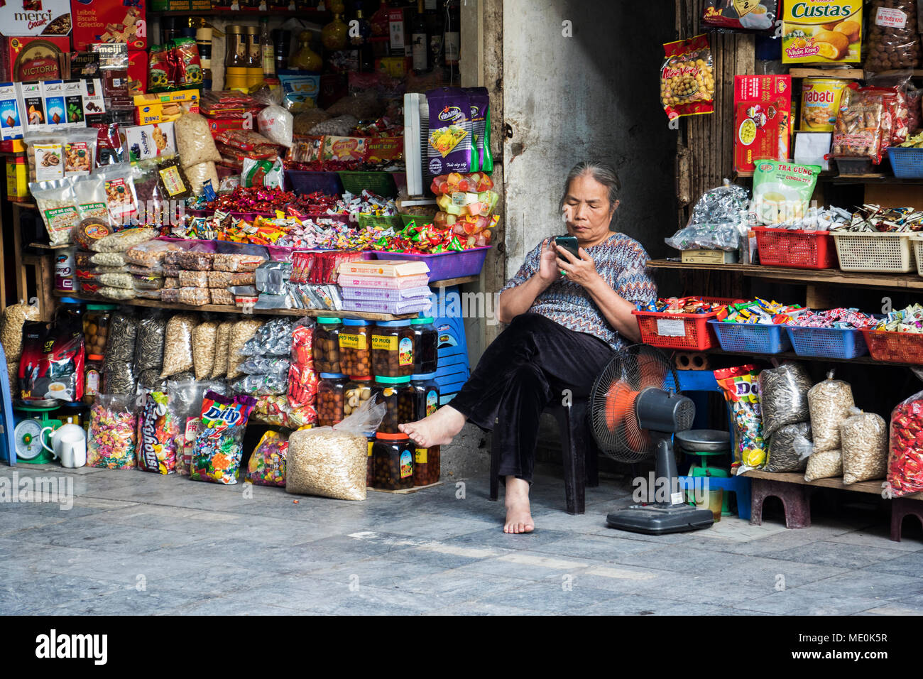 Female vendor sitting outside her shop with bare feet using her smart ...