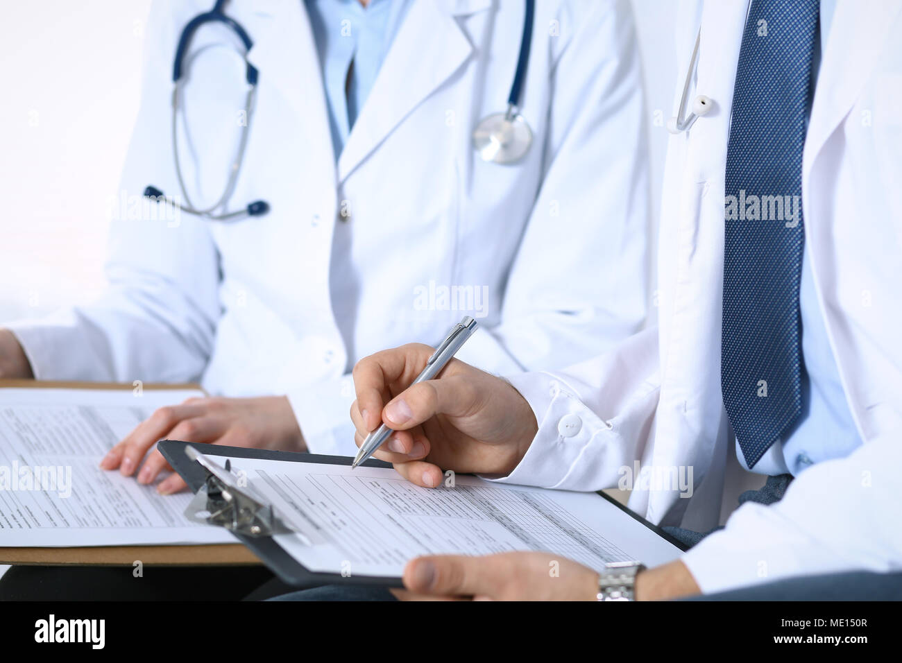 Two unknown doctors filling up medical form on clipboard, just hands ...