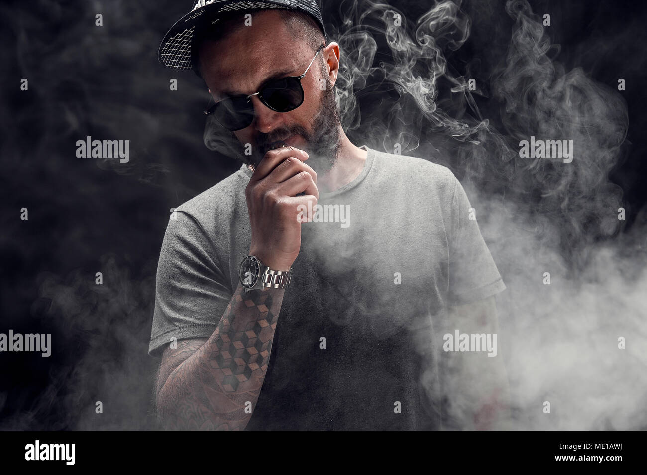 bearded male dressed in a grey shirt, sunglasses and baseball cap ...