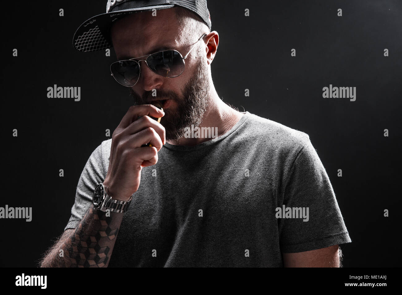 bearded male dressed in a grey shirt, sunglasses and baseball cap ...