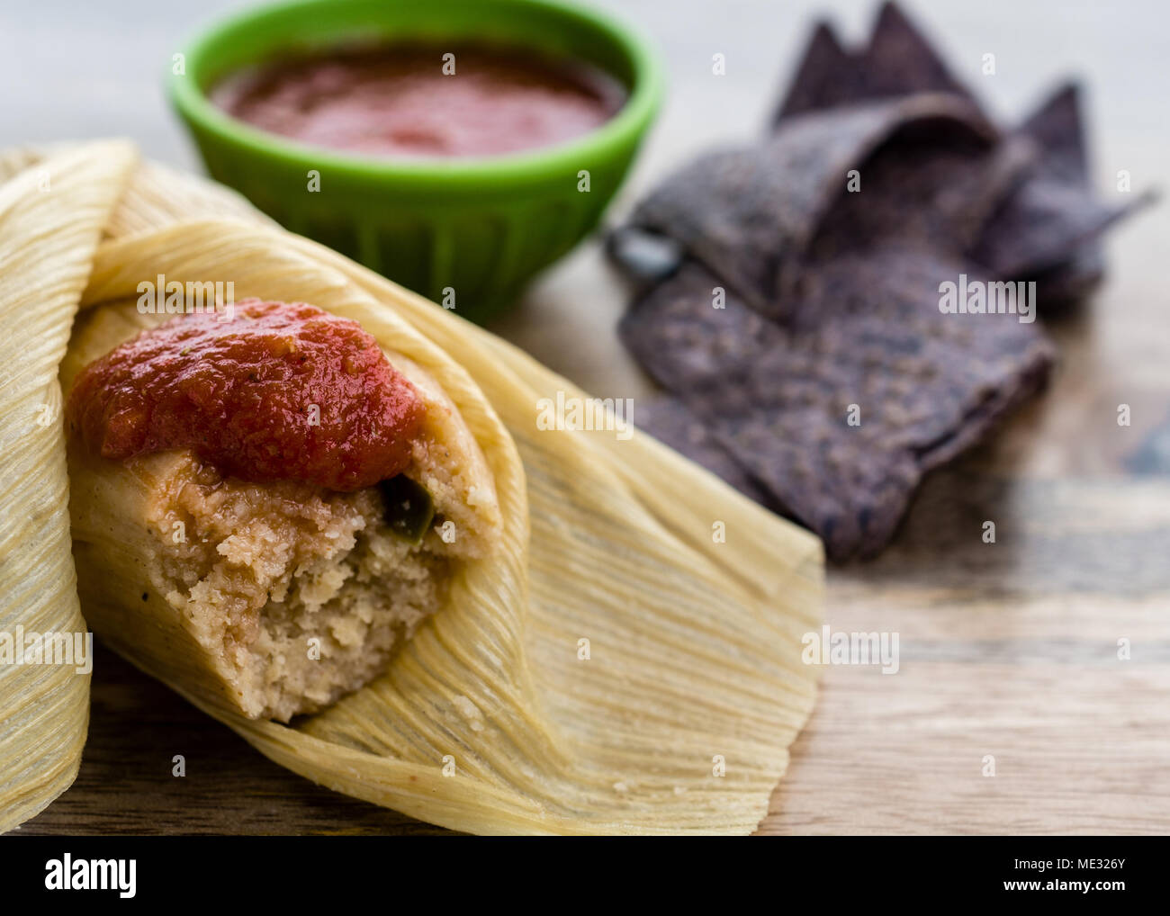 Partly unwrapped tamale served with blue corn tortillas and tomato ...