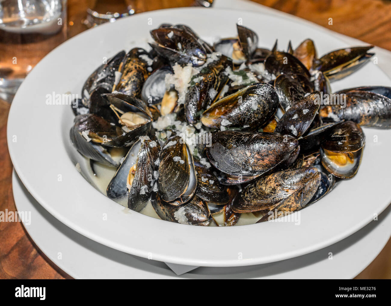 Steamed mussels in white plate garnished with garlic and accompained by ...