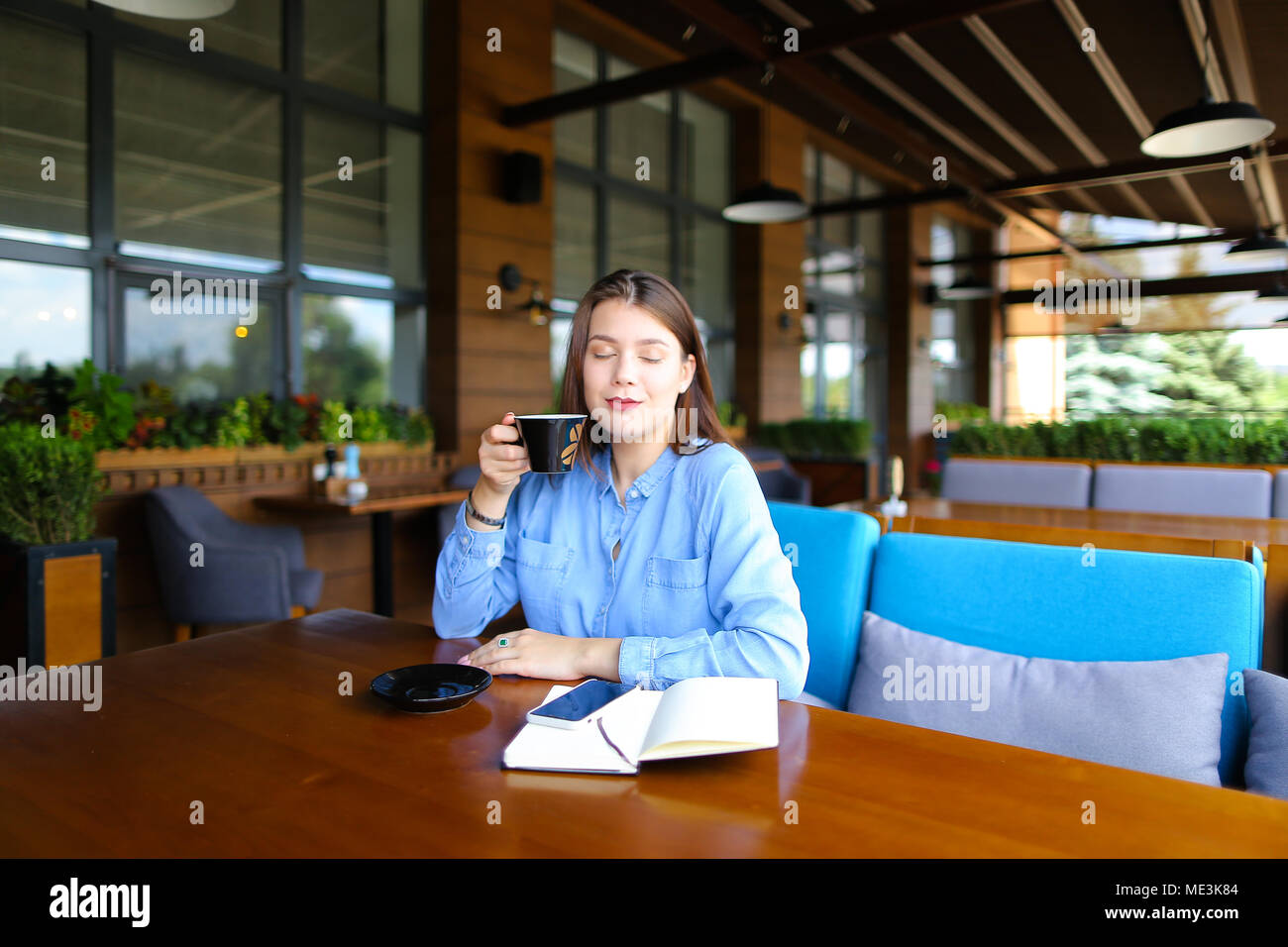 Caucasian female person sitting at cafe with smartphone and notebook ...