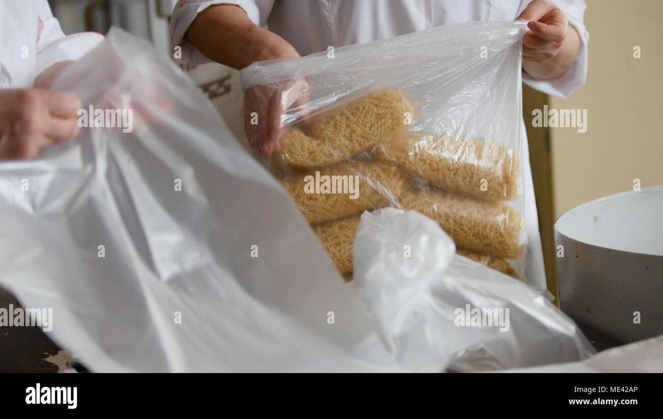 Worker packaging macaroni from the conveyor belt in a pasta factory ...