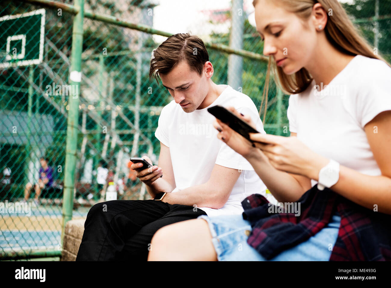 Expressionless young couple in the park using smartphones with no ...