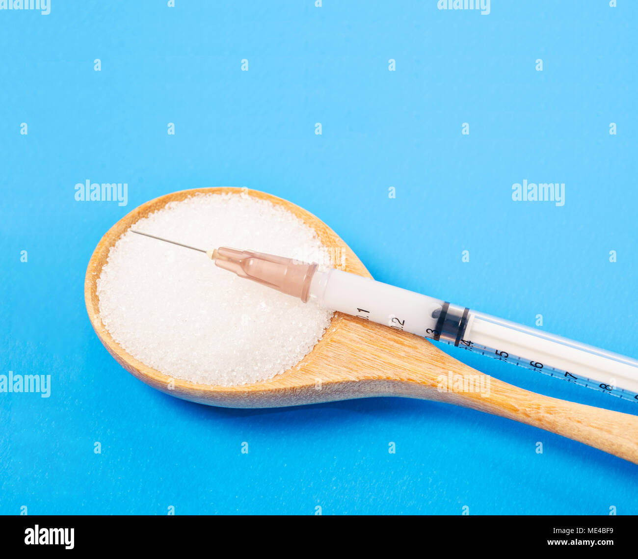 insulin in syringe and white sugar in wooden spoon on blue background ...