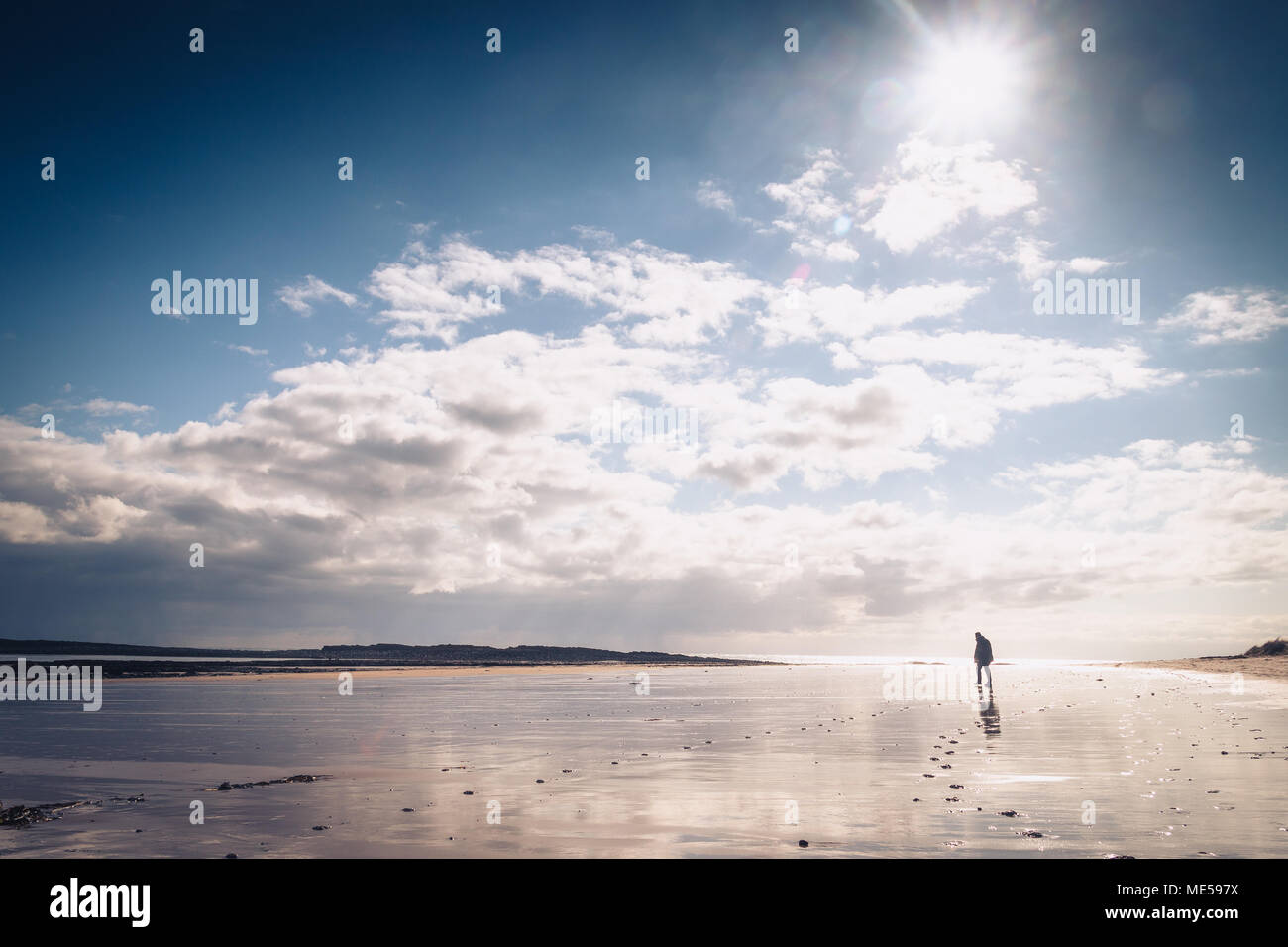 Sun shining on the beach and reflecting a solo person leaving ...