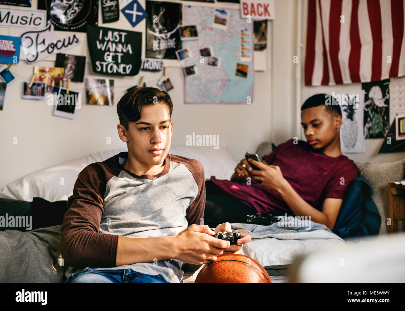 Teenage boys hanging out in a bedroom playing a video game and using a ...