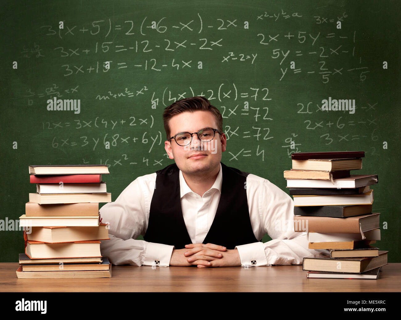 A young ambitious teacher in glasses sitting at classroom desk with ...