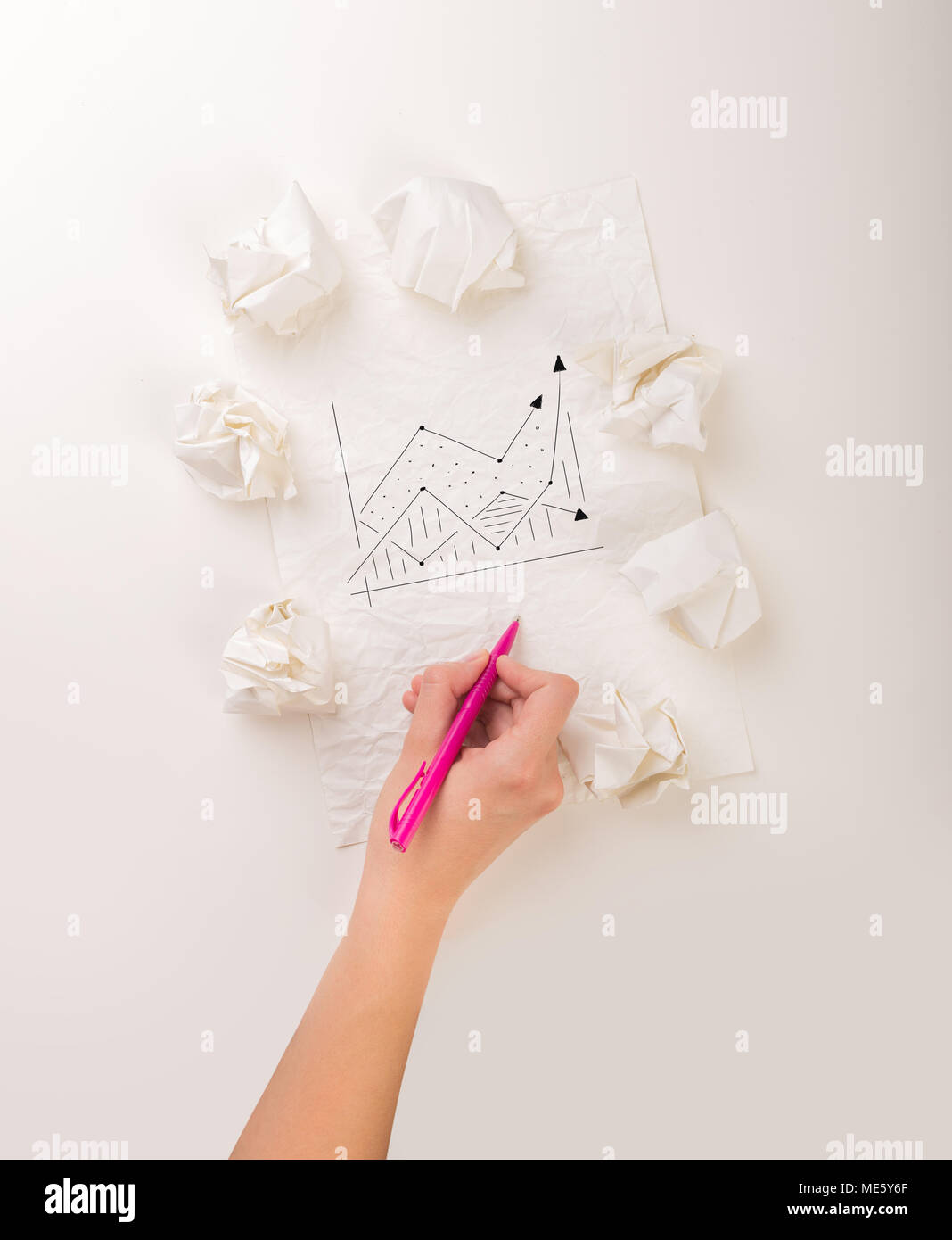 Female hand next to a few crumpled paper balls drawing a progress chart ...
