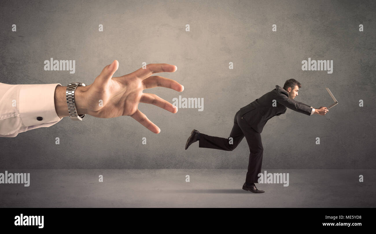 Young miniature businessman running from a big hand with grey ...