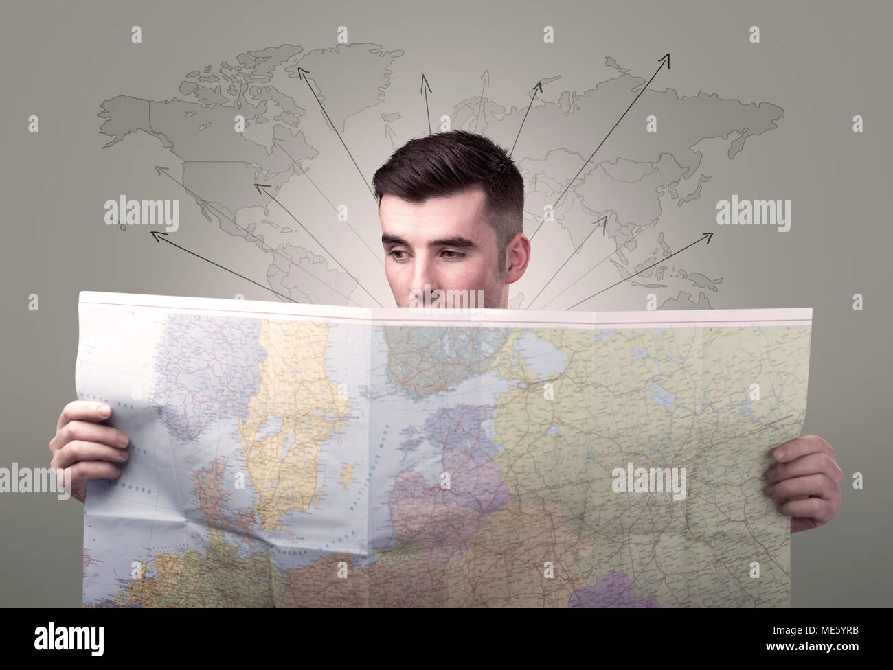 Handsome young man holding a map with world map and arrows behind him ...