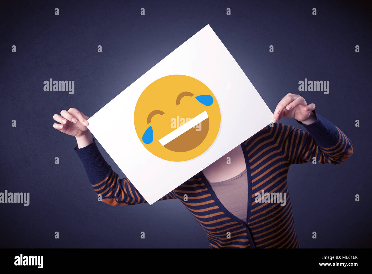 Young casual woman hiding behind a laughing emoticon on cardboard Stock ...