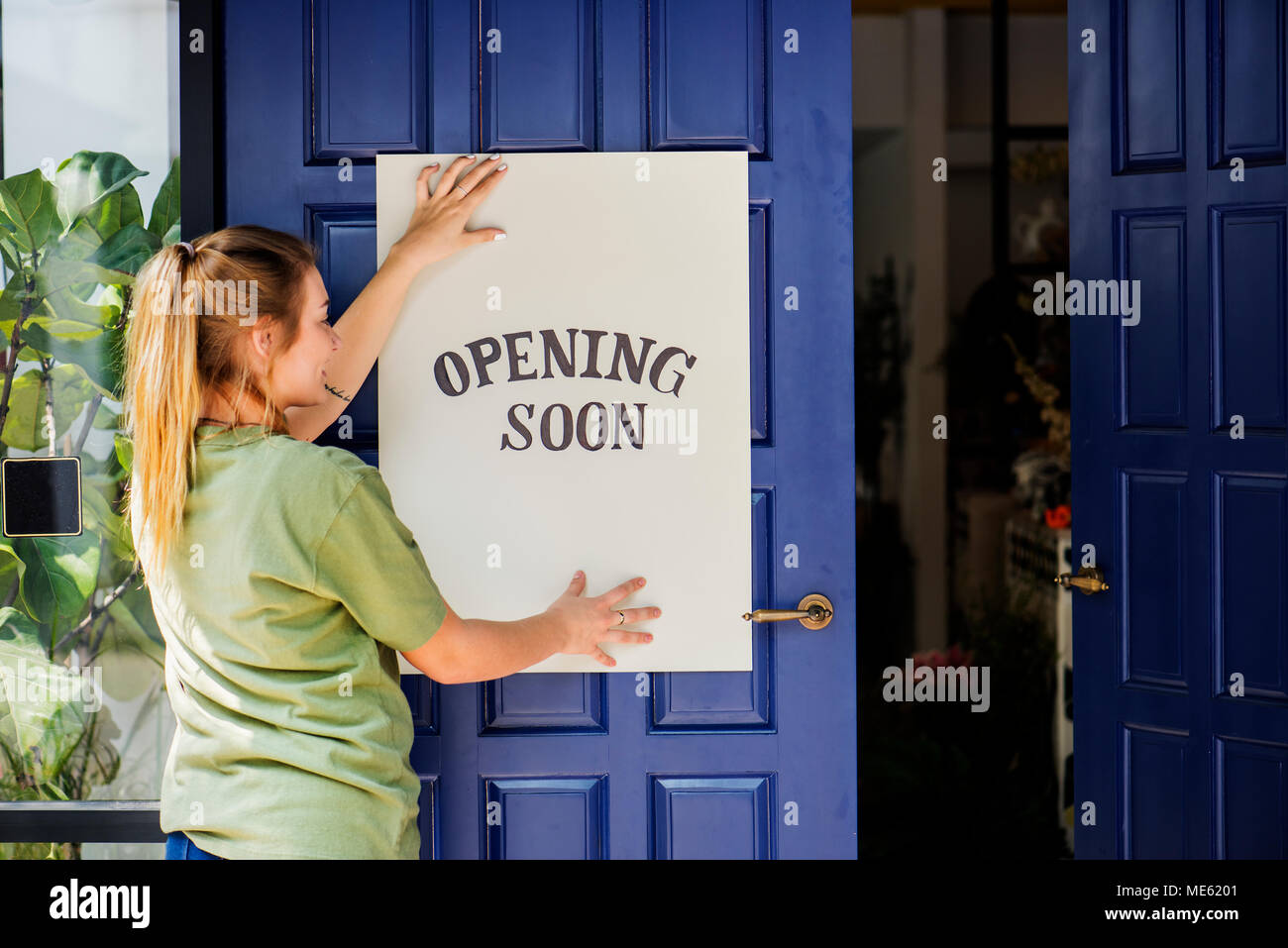 Woman putting on store opening soon sign Stock Photo - Alamy