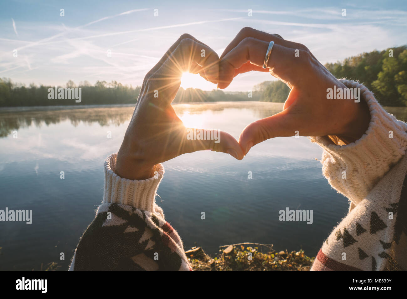 Close up on female's hands making a heart shape finger frame on lake ...