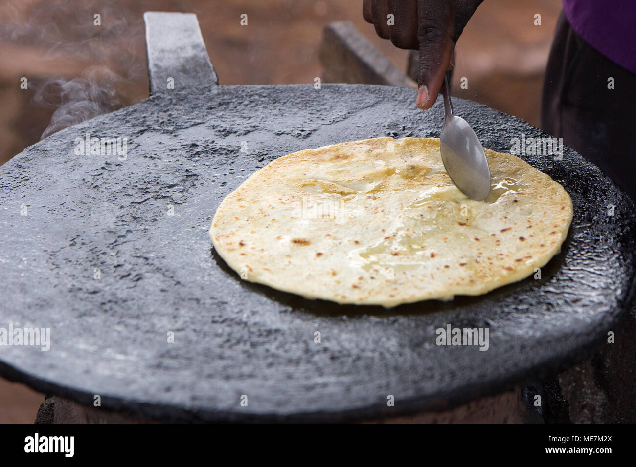 A flatbread called "chapati" being fried and folded with a spoon by a ...