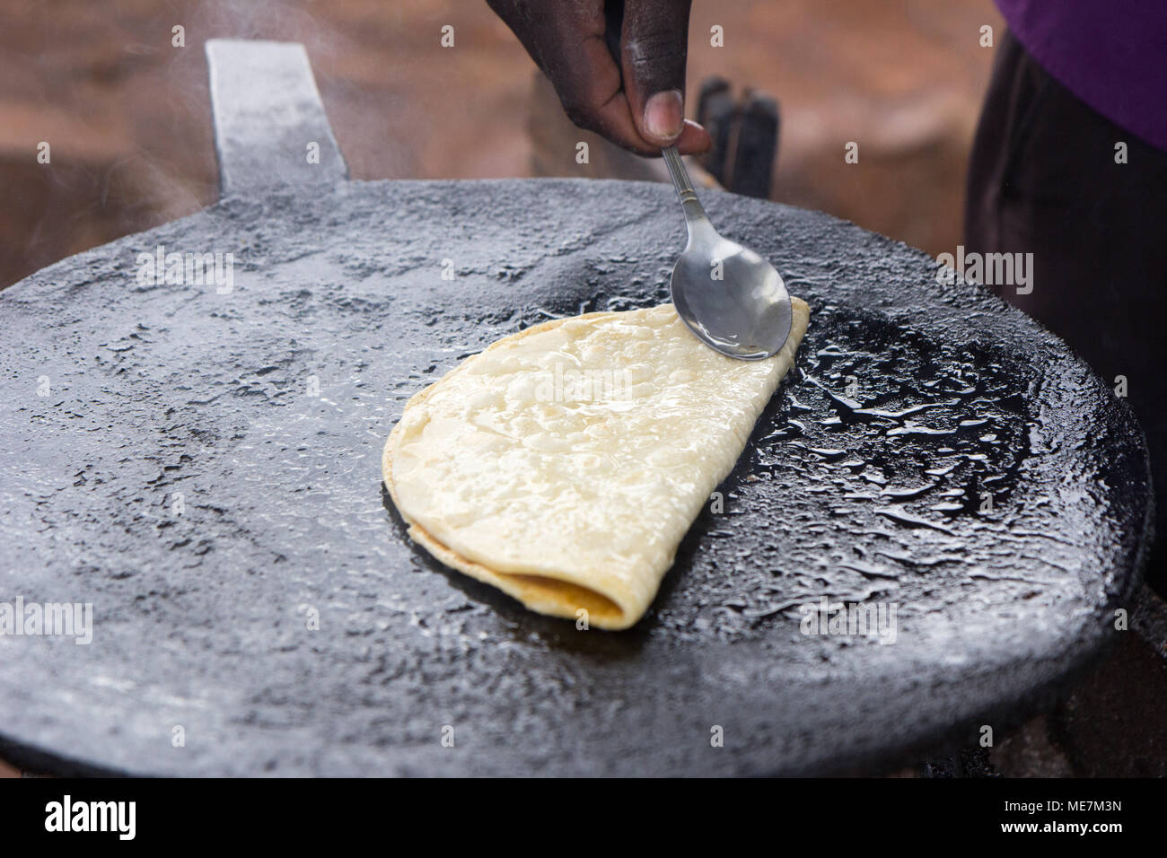 A flatbread called "chapati" being fried and folded with a spoon by a ...