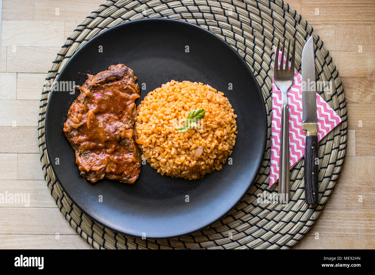 Steak with tomato sauce and bulgur rice pilav / pilaf in a black plate ...