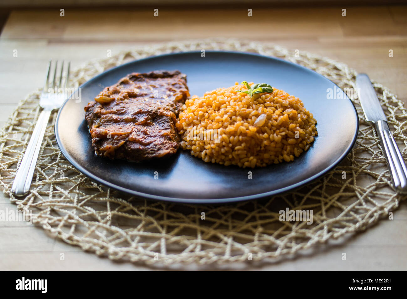 Steak with tomato sauce and bulgur rice pilav / pilaf in a black plate ...