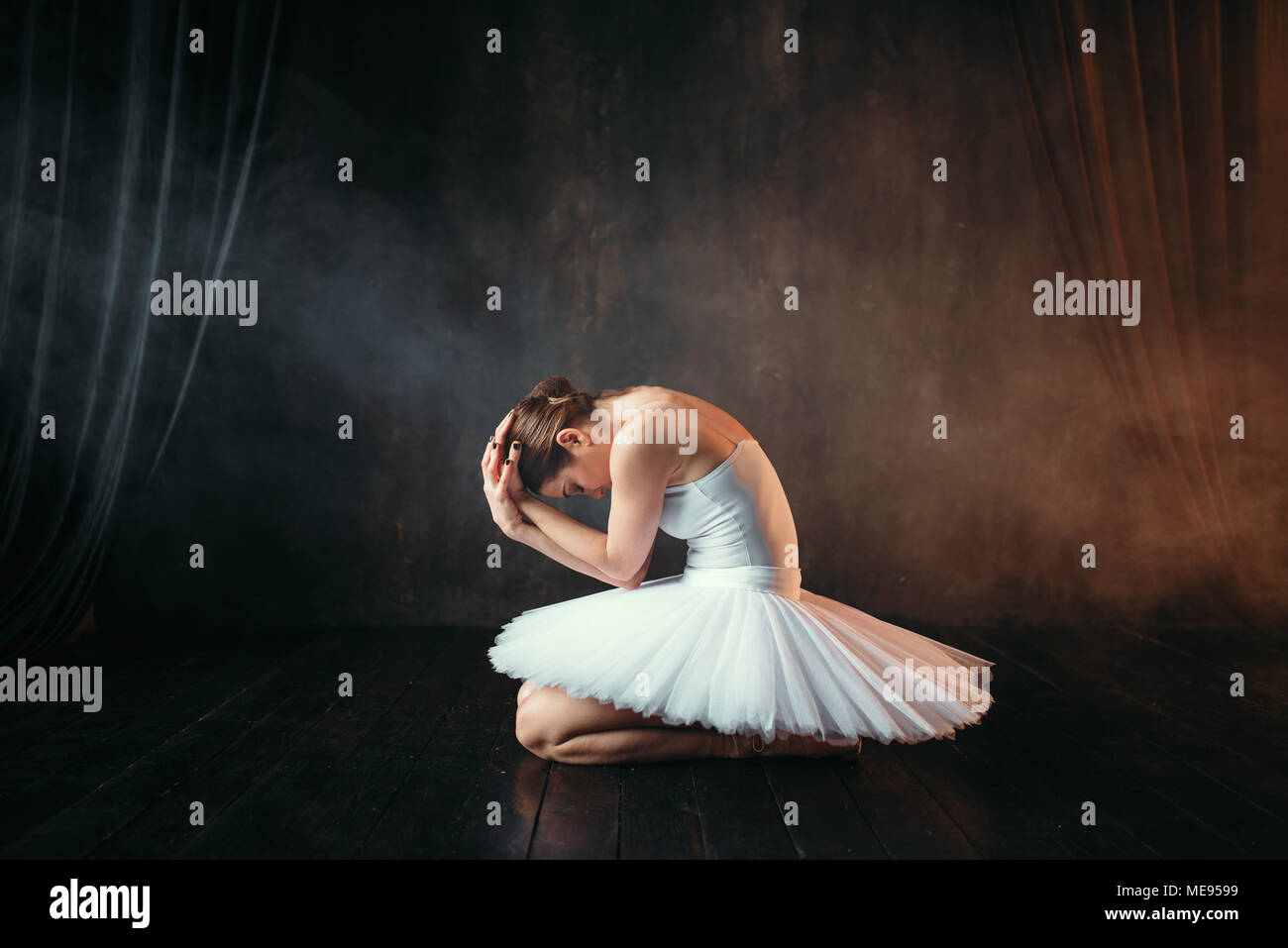 Ballerina in white dress sitting on theatrical stage, side view ...