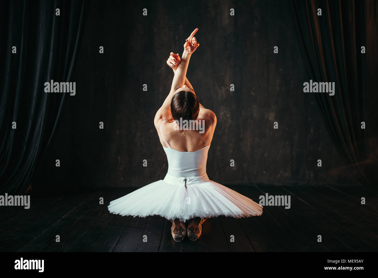Female classical ballet performer in white dress sitting on the floor ...