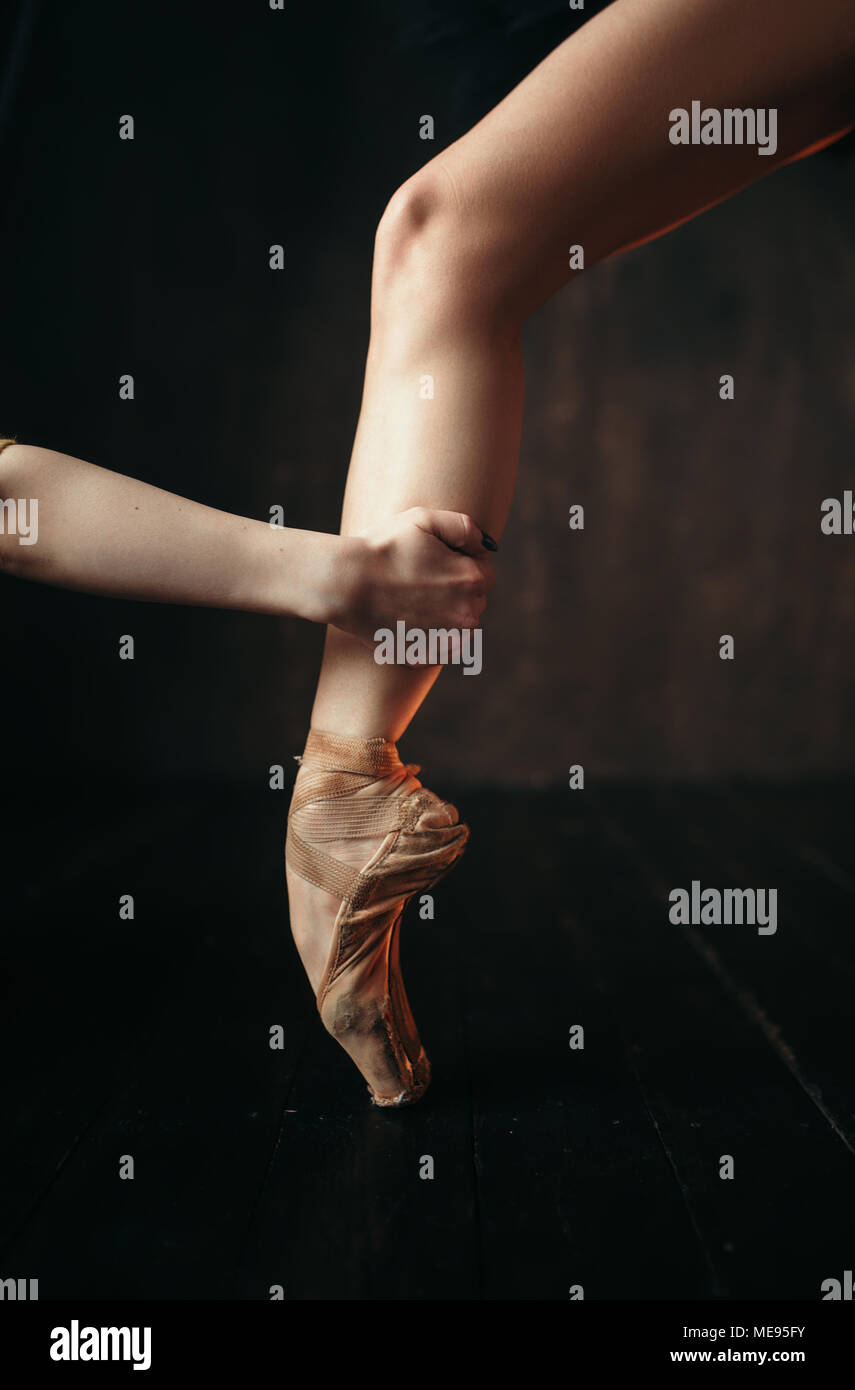 Ballerina hand holds the foot in pointe shoes, black wooden floor ...