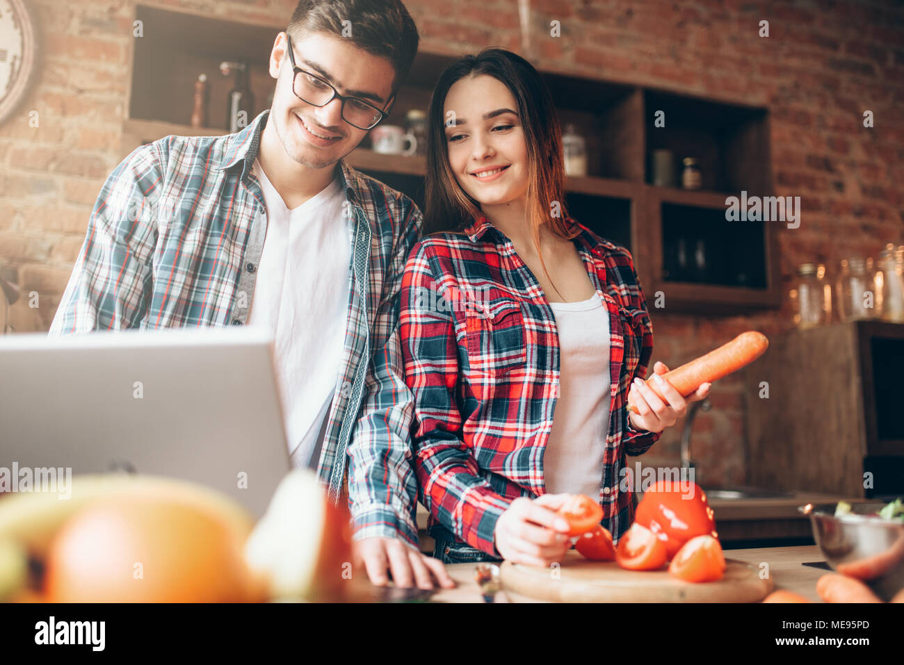 Happy couple looks at a recipe in laptop, vegetable salad cooking on ...