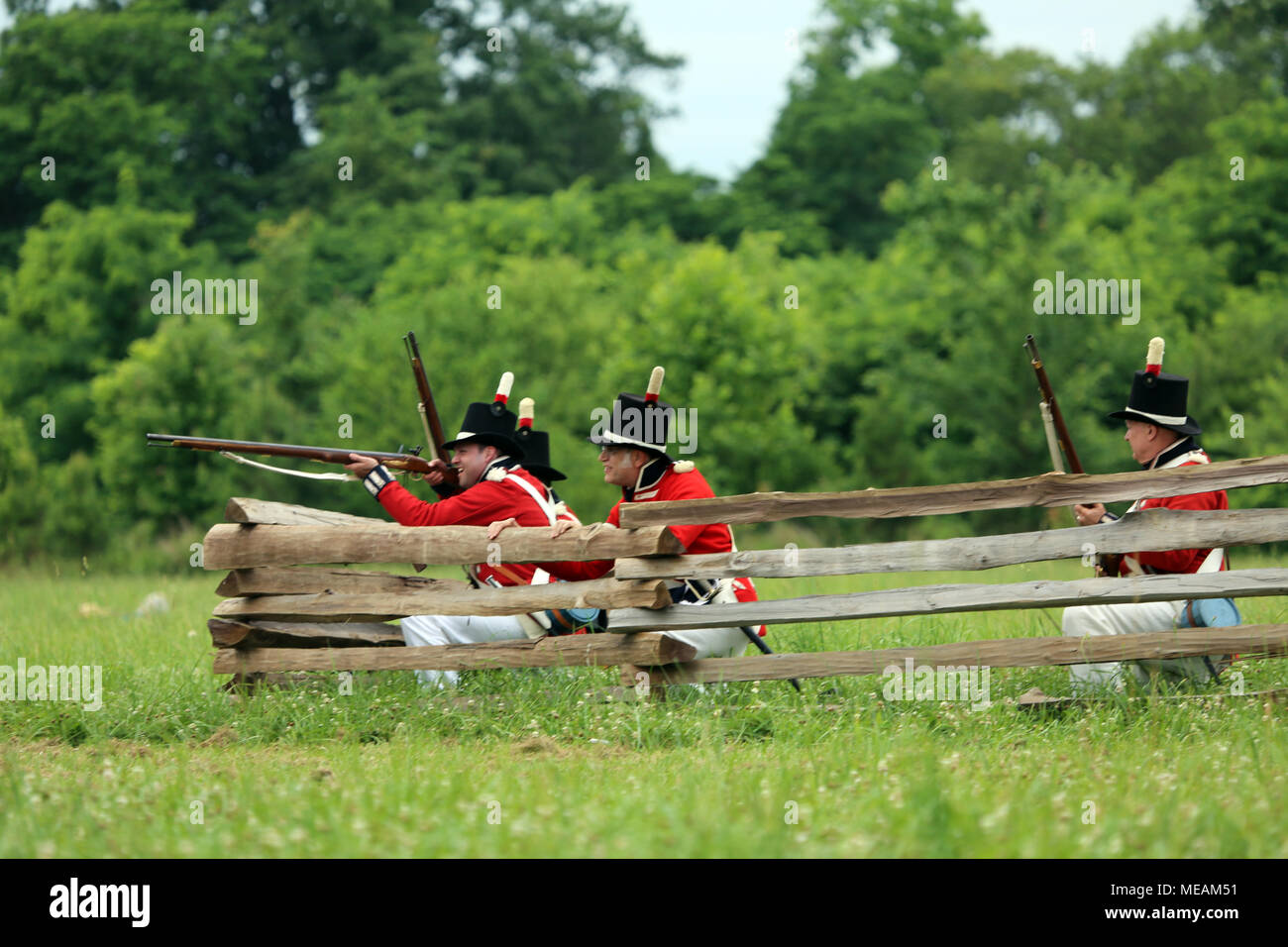 British soldier reenactors firing muskets behind wooden fence duirng ...