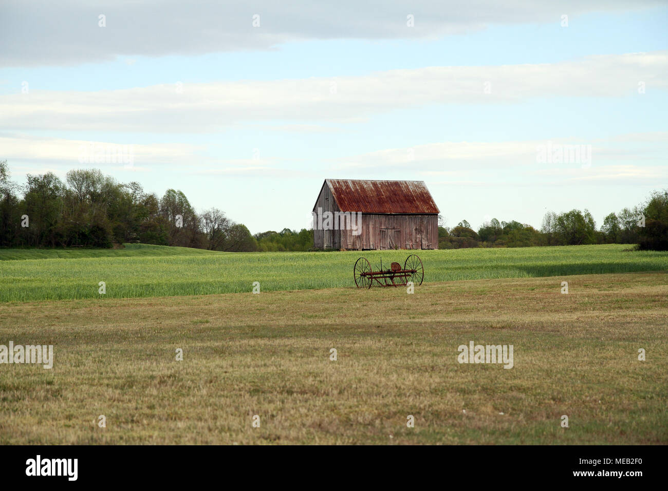 old rusty horse drawn cultivator with farm field and tobacco barn in ...