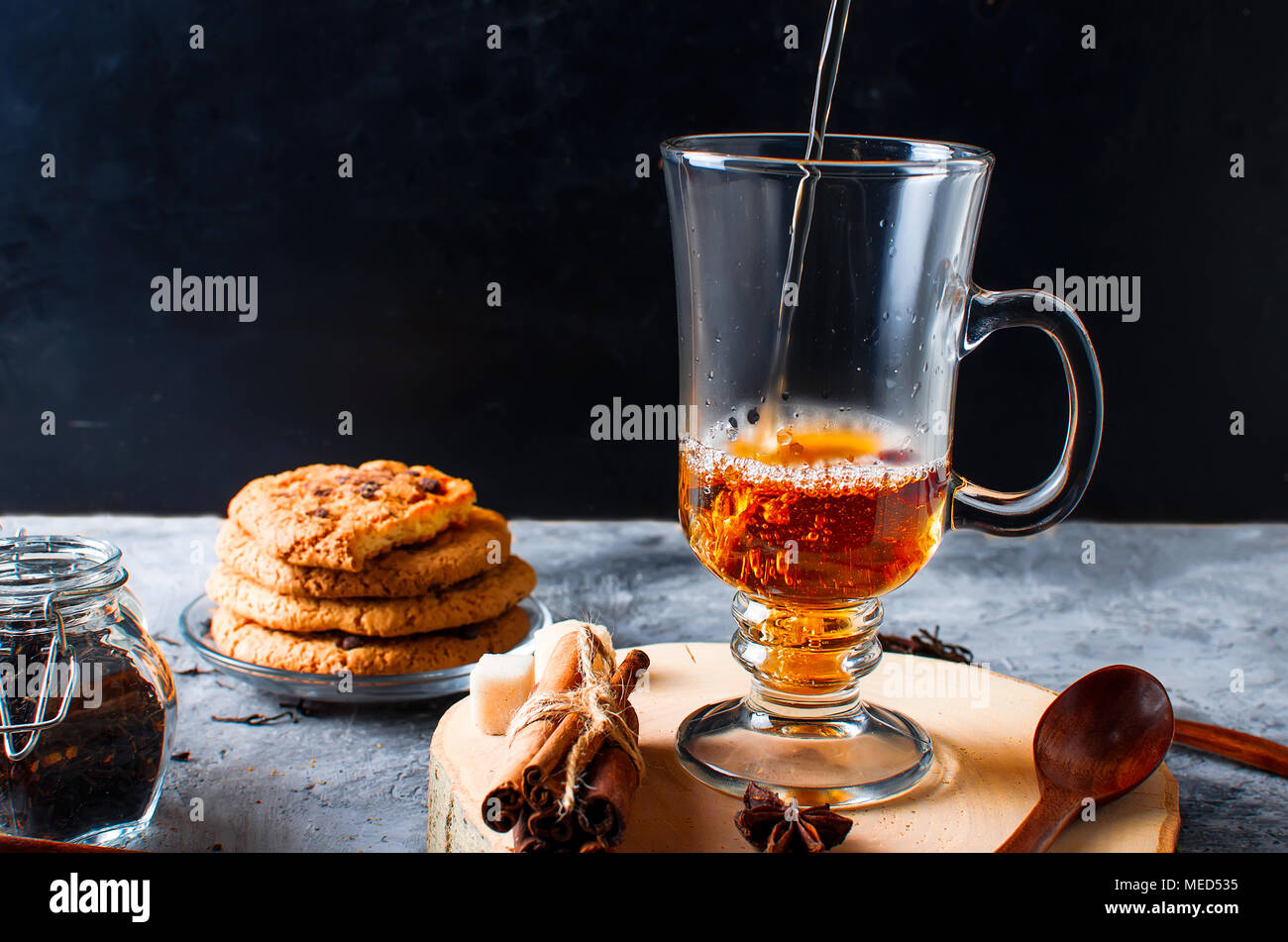 Pouring tea in cup on dark background, Cup of tea, biscuits, spices for ...