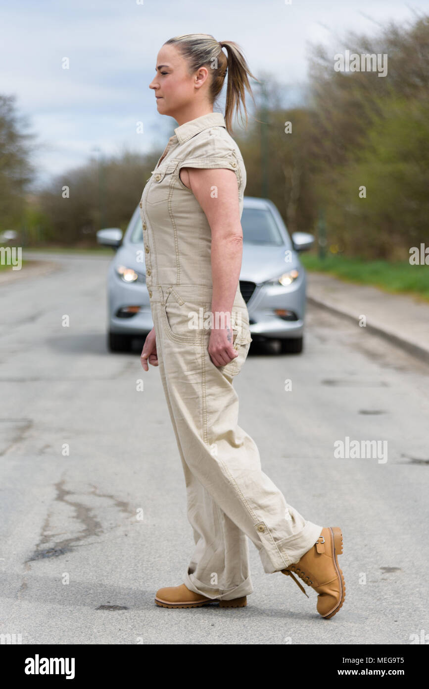 Woman crossing the road, with a car approaching behind her Stock Photo ...