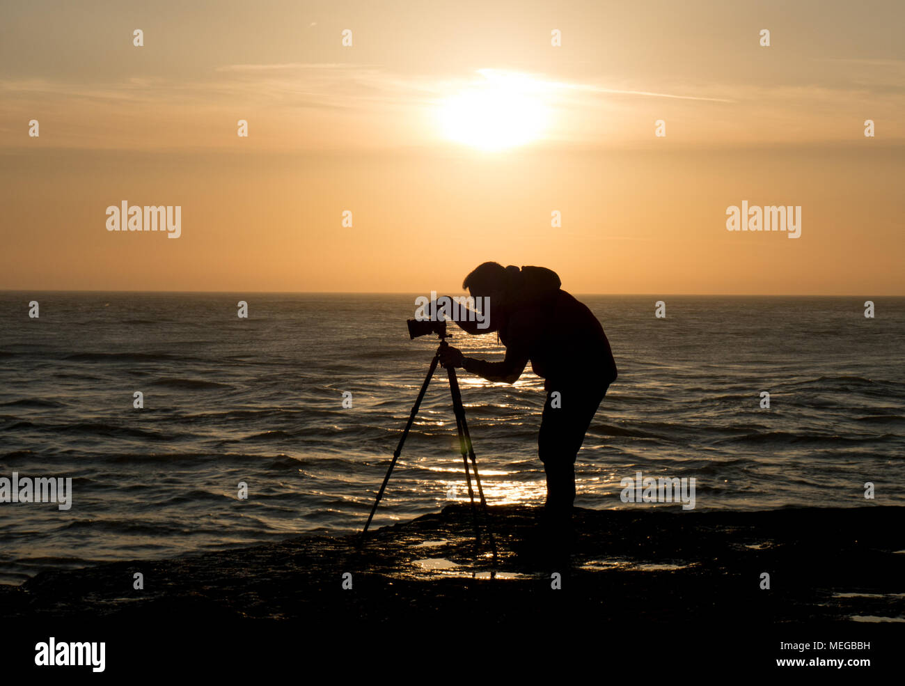 A photographer composes his shot carefully at sunset near the sea Stock ...