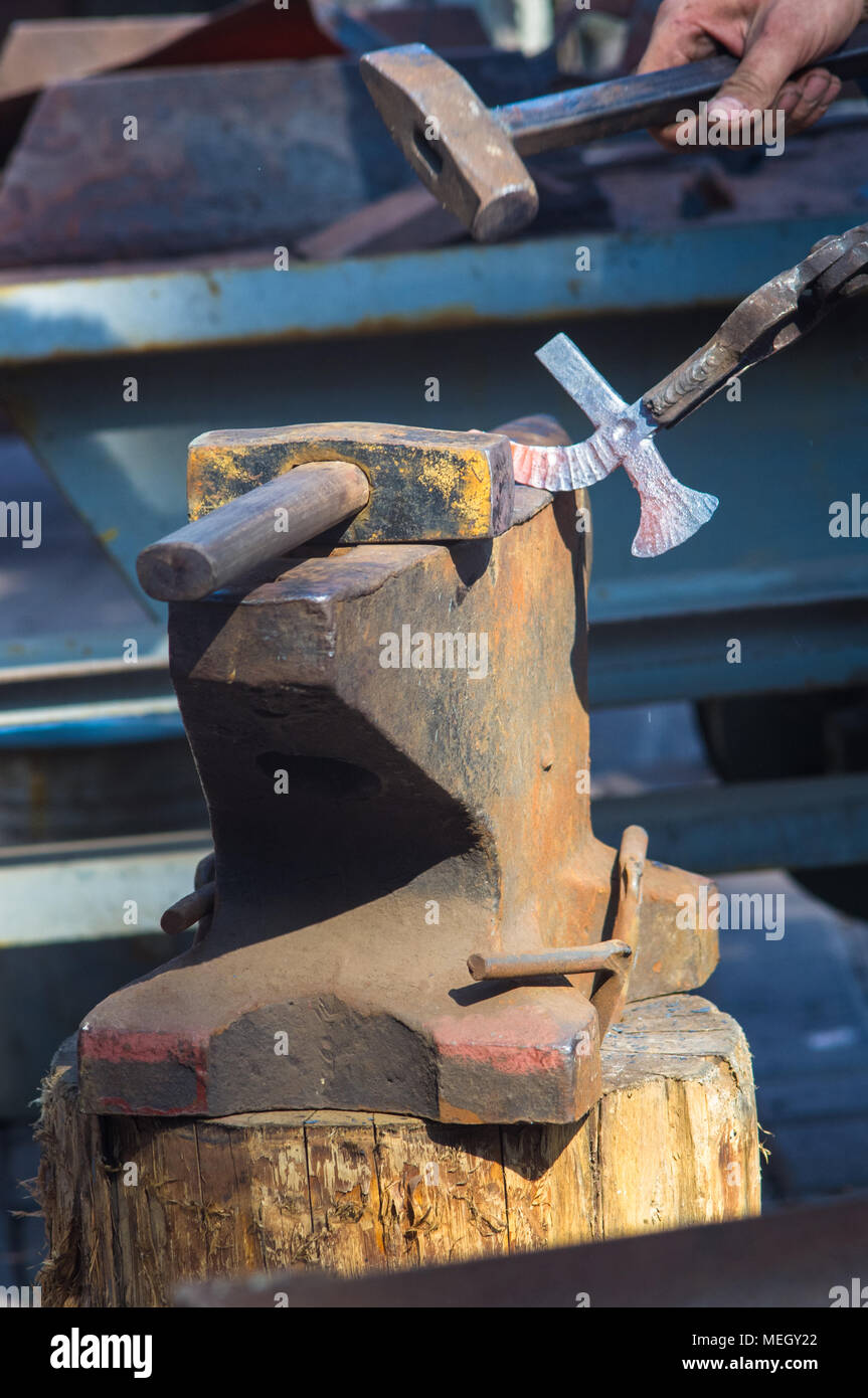 blacksmith performs the forging of hot glowing metal on the anvil ...