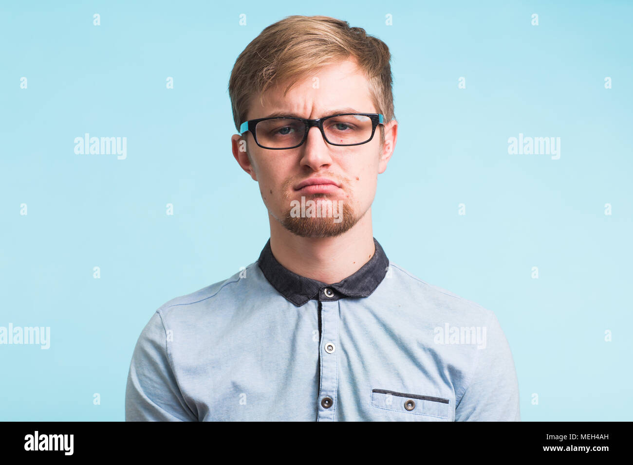 Portrait of young funny sad man wears spectacles isolated over blue ...