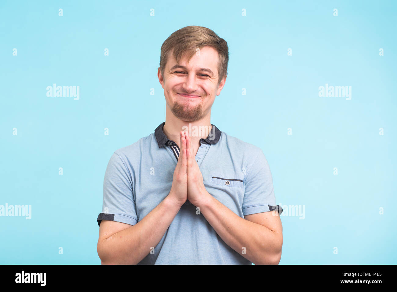 Handsome young man with hands together in praying gesture, expressing ...