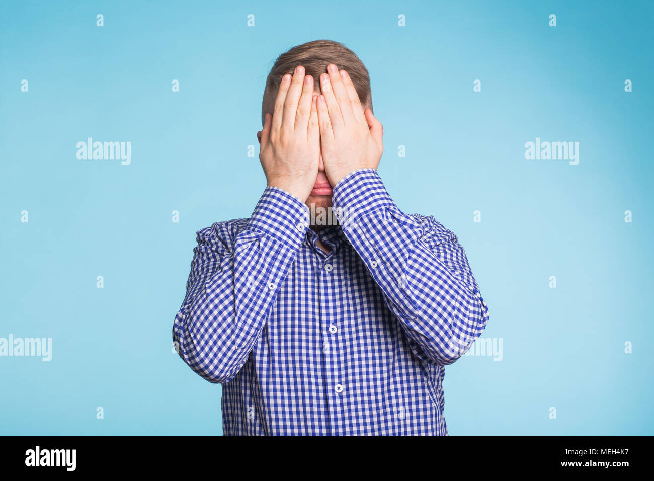 man covered his face with hand on blue background Stock Photo - Alamy