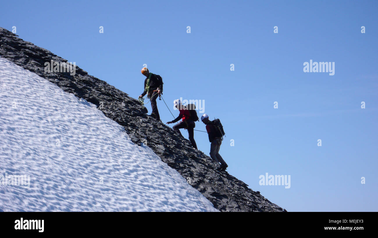 mountain guide leading two male clients to a rocky ridge and onwards to ...